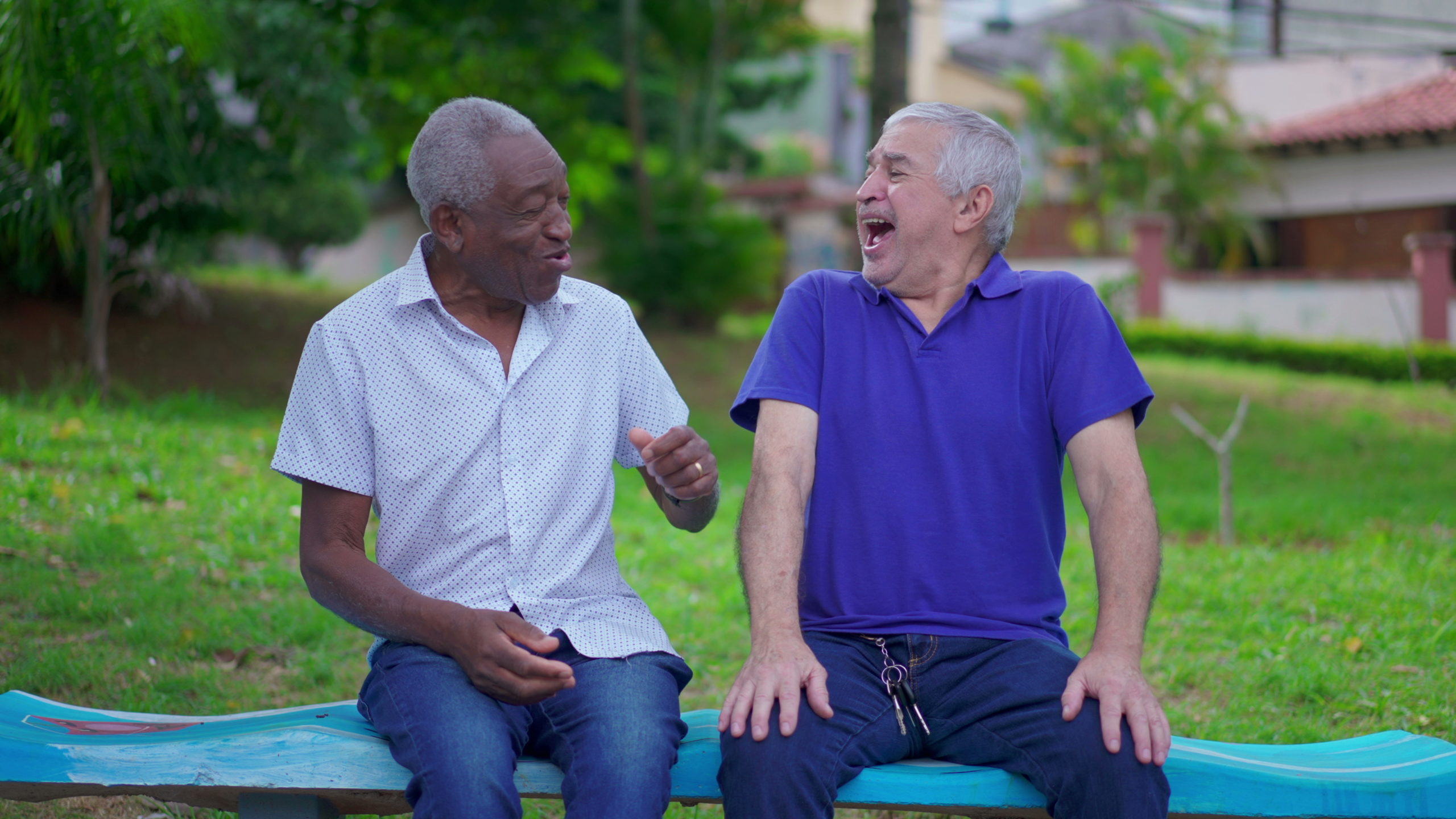 Two diverse senior talking and laughing sitting on park bench in Brazil ...